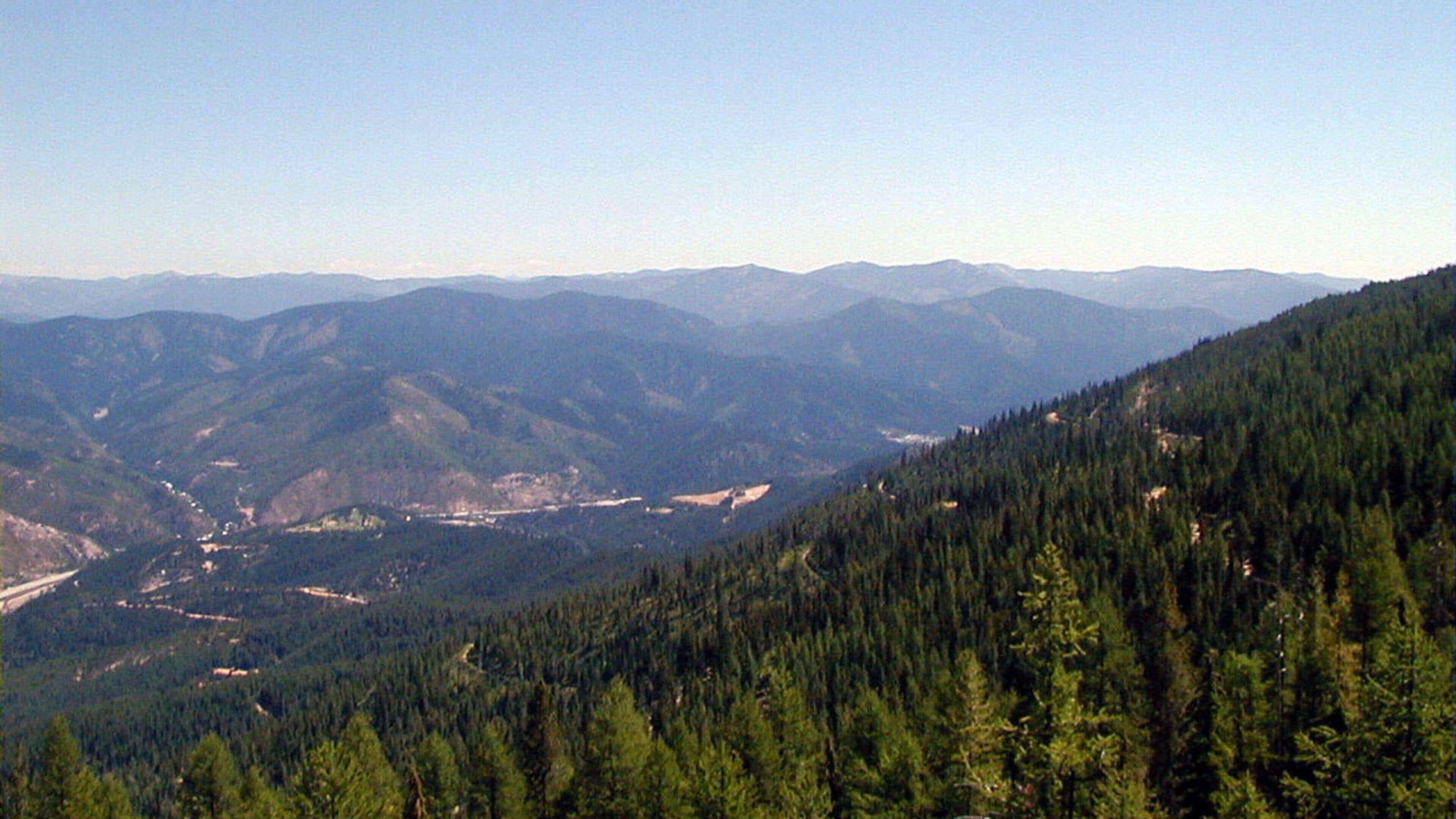 Paisagem montanhosa com florestas densas e uma estrada sinuosa.