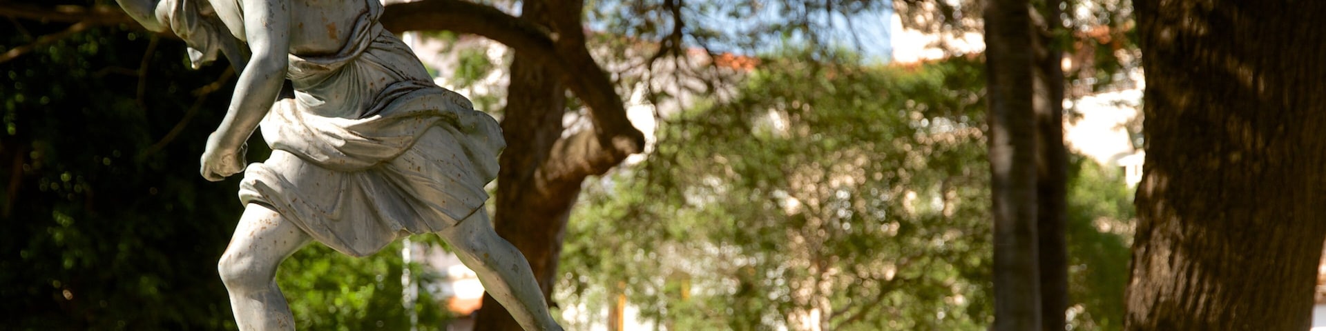 Uma estátua de uma figura em movimento, rodeada por árvores e pessoas ao fundo.