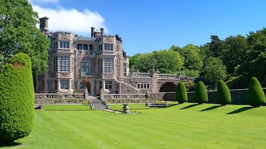 Um grande edifício histórico de pedra com um jardim formal e sebes aparadas.