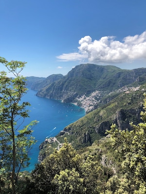 Paisagem costeira com mar azul cristalino, colinas verdes e uma pequena cidade aninhada entre montanhas.