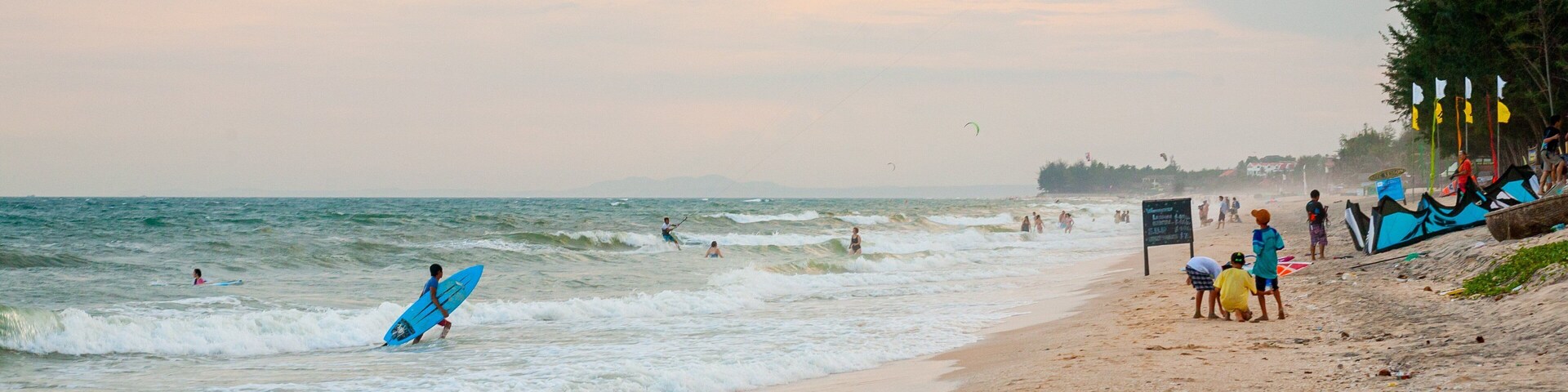 Uma praia com ondas, pessoas e uma pipa.