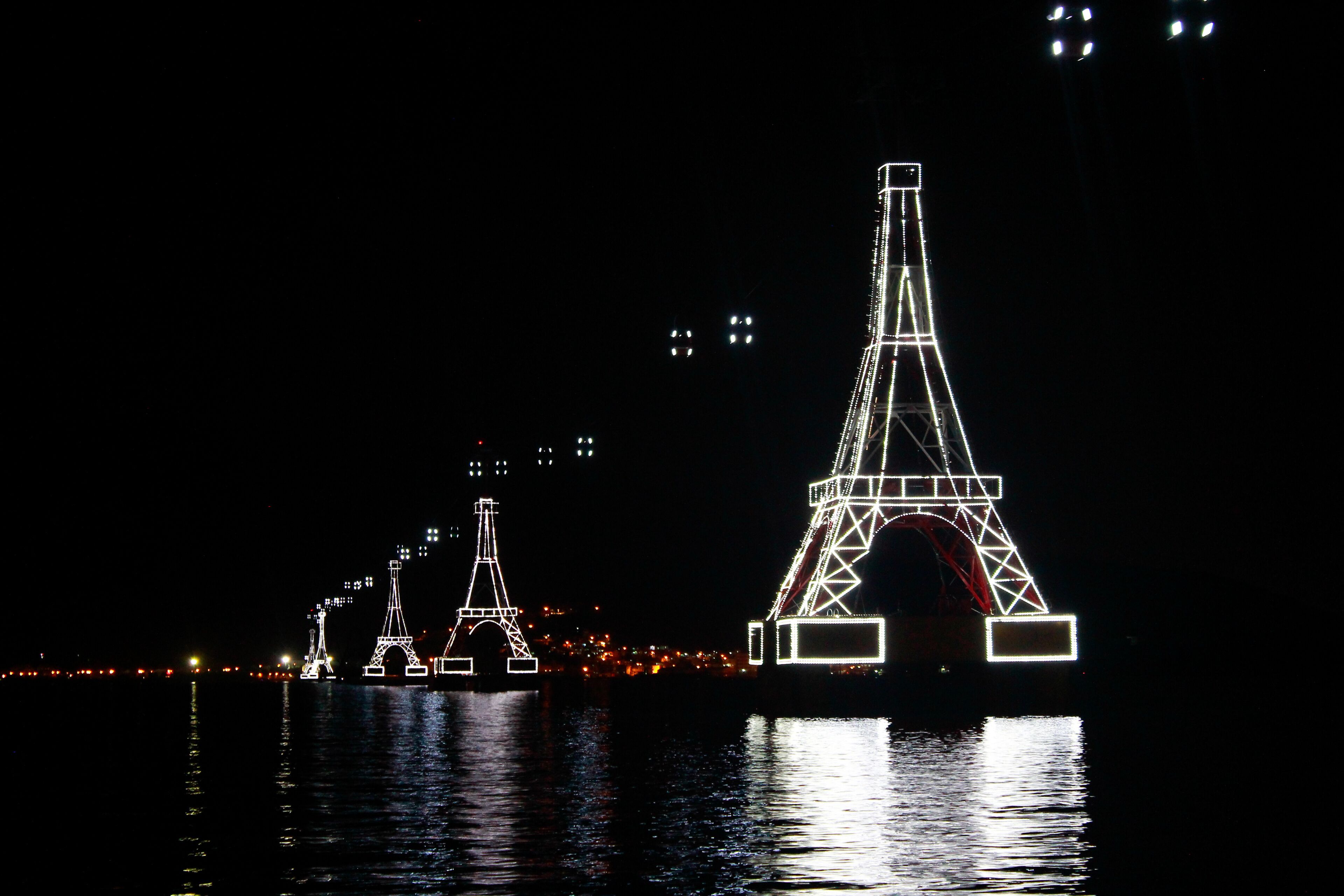 Réplicas iluminadas da Torre Eiffel sobre a água, à noite.