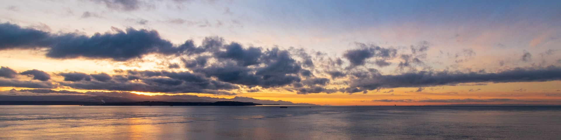 Mar calmo ao pôr do sol, com terra à distância e céu nublado.