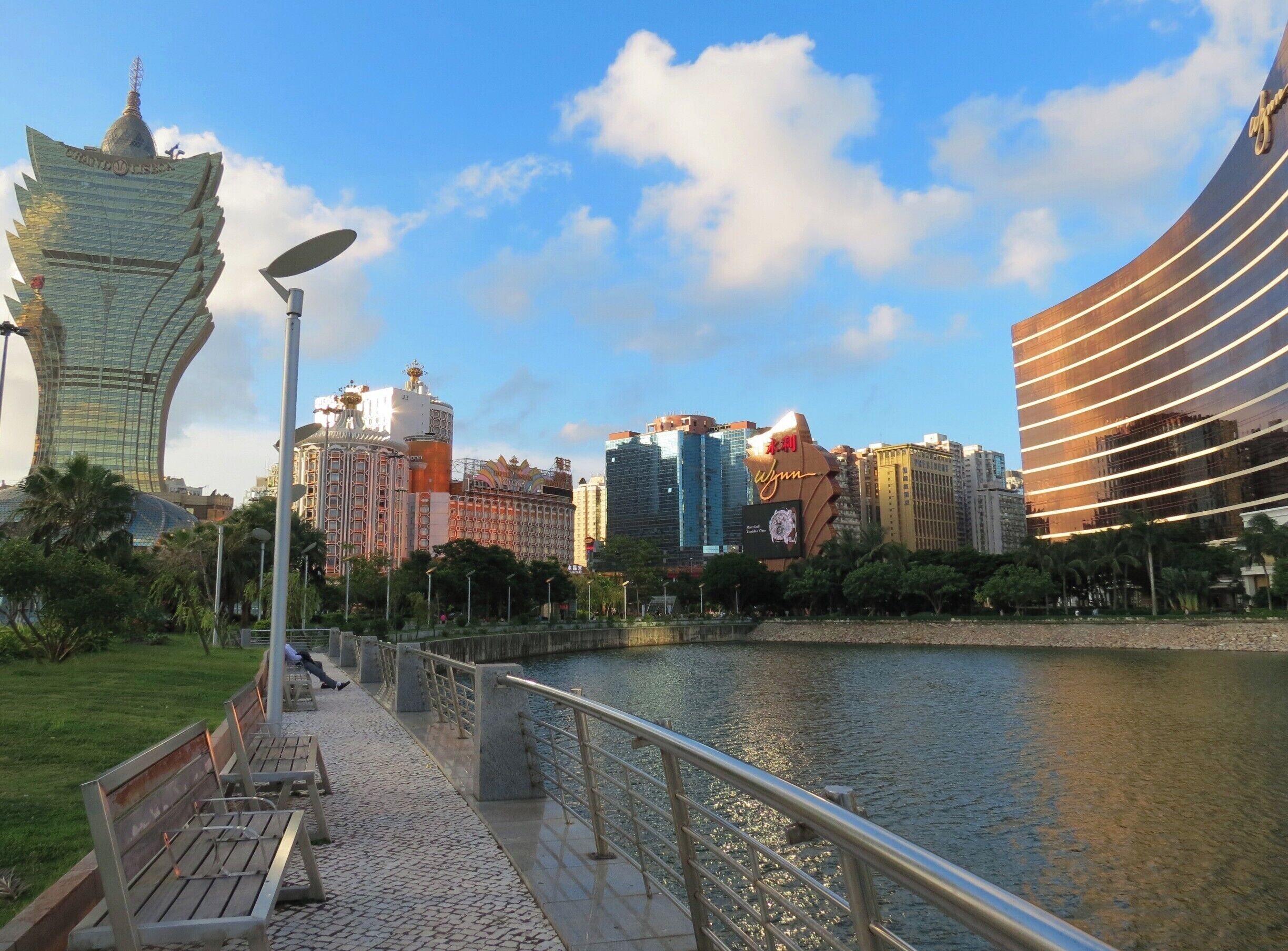 Um passeio à beira do rio com bancos, uma estrutura peculiar semelhante a um pagode e um edifício moderno com fachada curva.