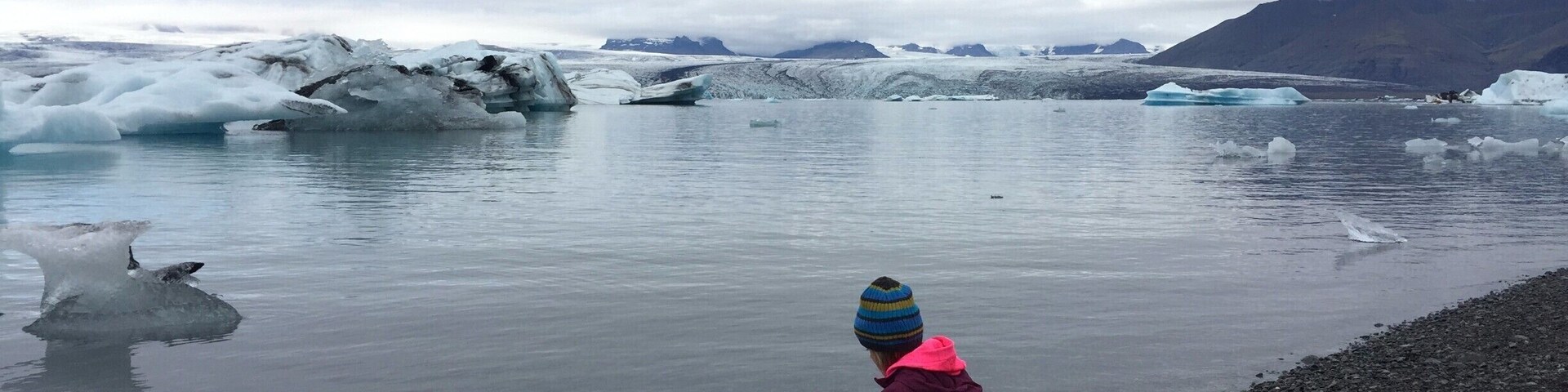 Uma criança em uma costa rochosa observa icebergs flutuantes em um fiorde glacial.