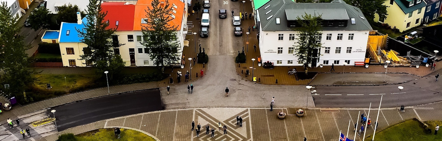 Vista aérea de uma cidade colorida, com uma praça central, uma estátua e um calçadão ao fundo.