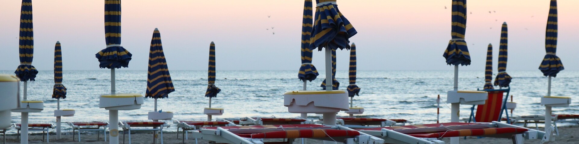 Guarda-sóis, espreguiçadeiras e o oceano ao pôr do sol.
