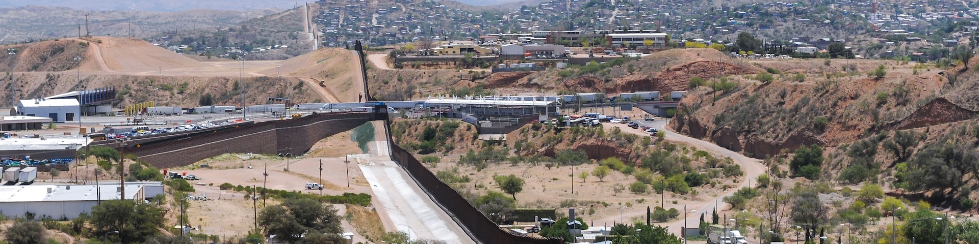 Uma barragem com vertedouro, uma autoestrada e uma cidade em uma paisagem desértica e montanhosa.