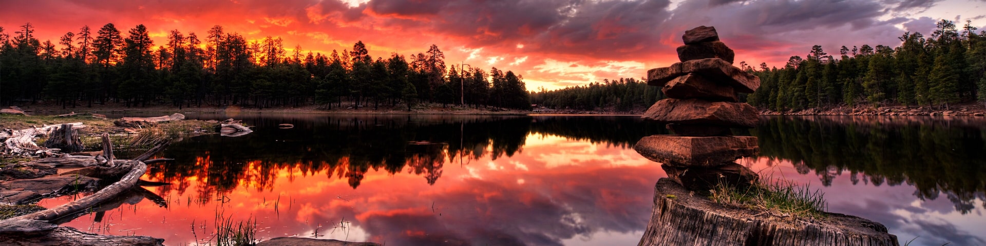 Um lago tranquilo com um pôr do sol, um amontoado de rochas e uma floresta ao fundo.