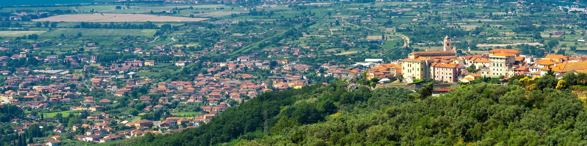 Uma vila costeira com uma igreja imponente em uma colina, rodeada por vegetação exuberante e vista para o mar.