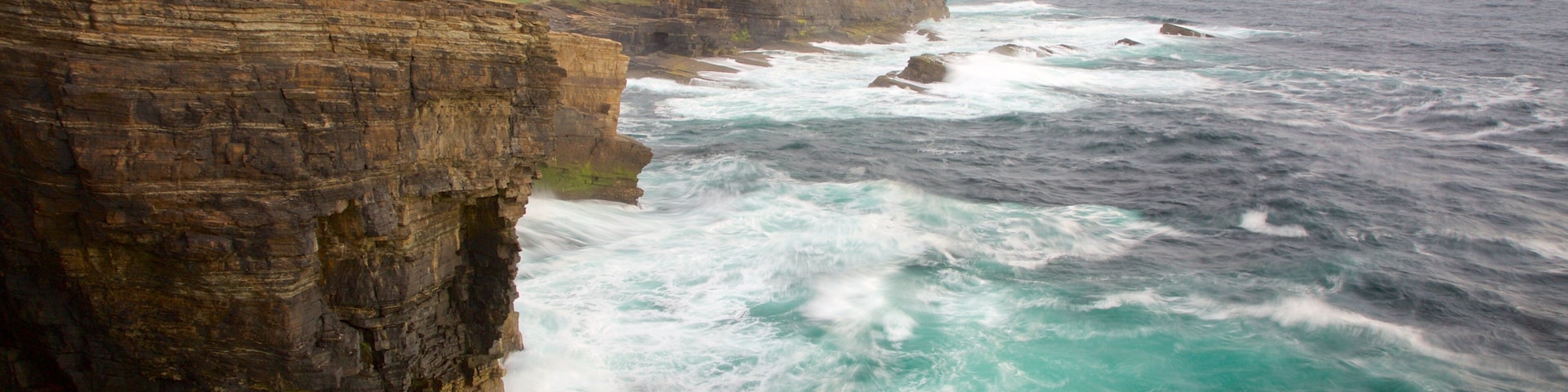 Costaço acidentado com falésias íngremes e ondas oceânicas agitadas.