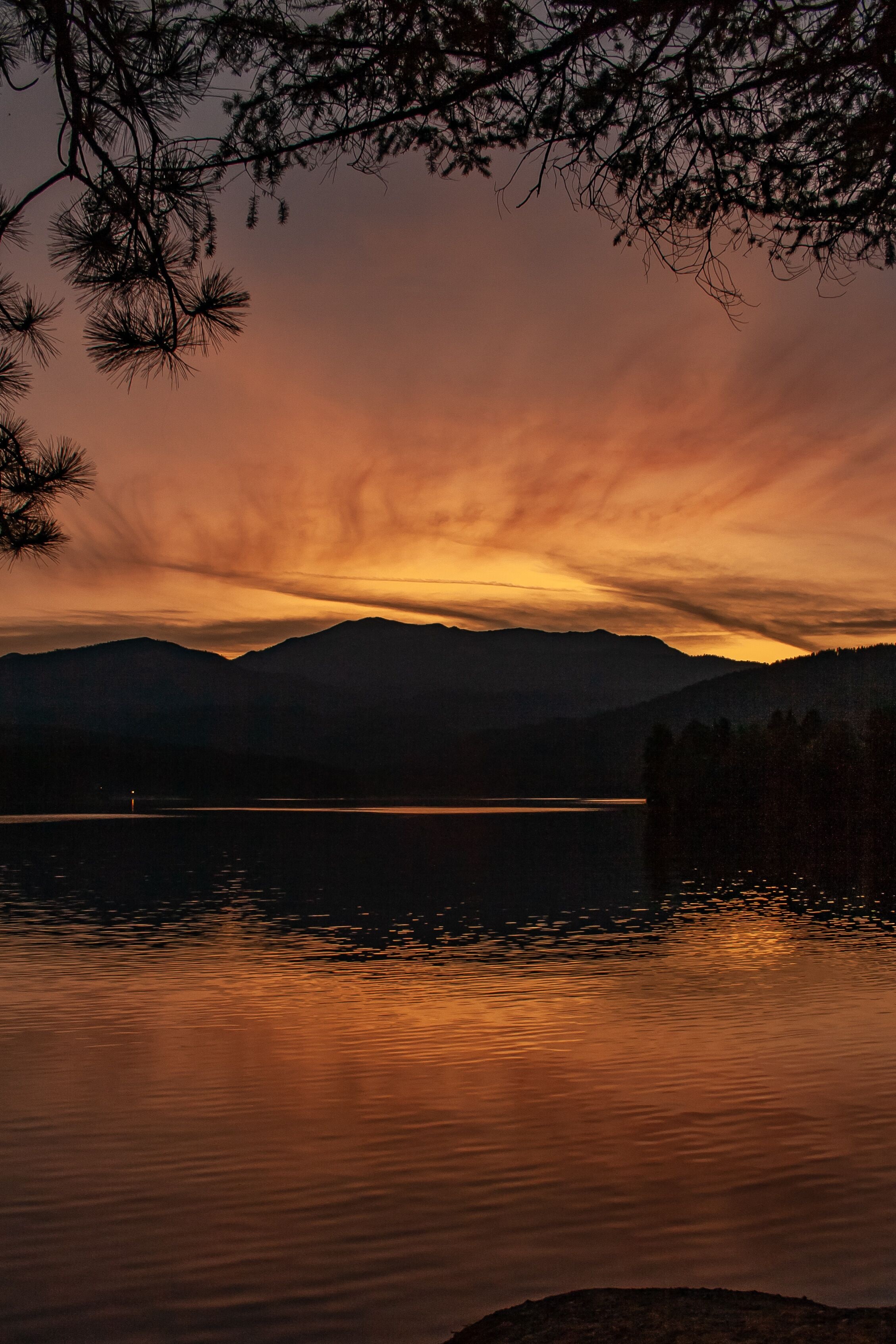 Um pôr do sol sobre um lago tranquilo com montanhas ao fundo.