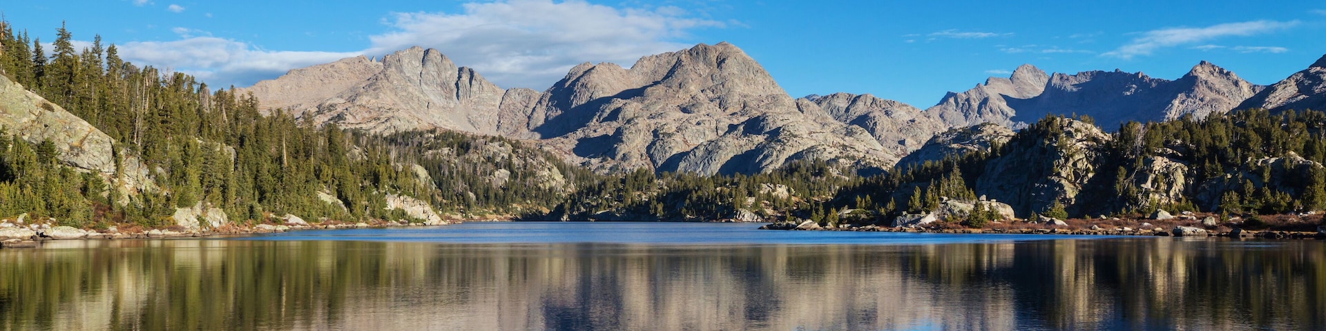 Um lago de montanha rodeado por montanhas rochosas e densas florestas.