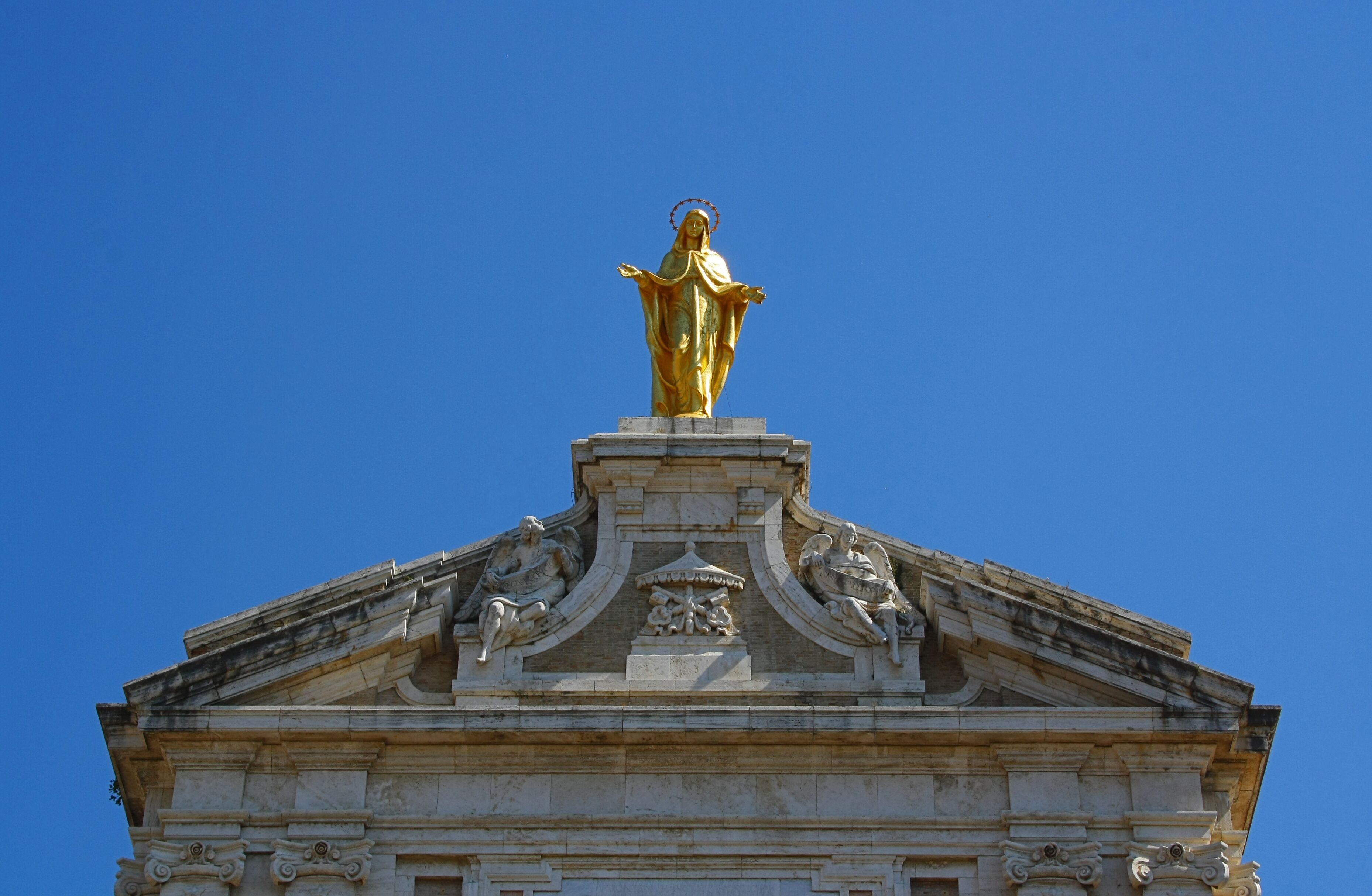 Estátua dourada no topo de um edifício clássico com esculturas elaboradas.