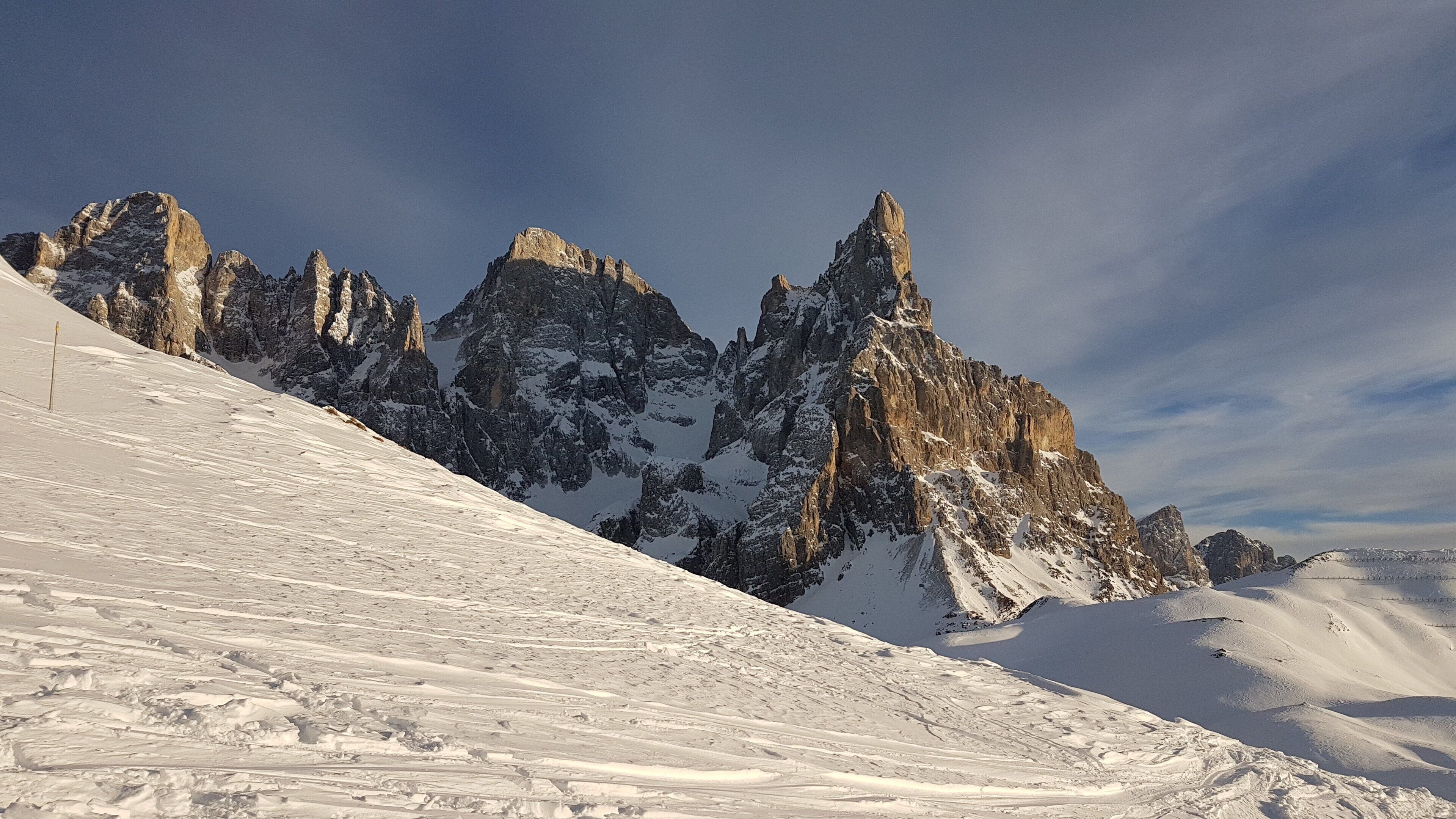Encosta de montanha coberta de neve, com picos rochosos e céu claro.