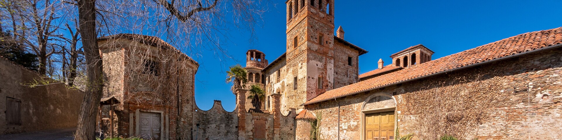 Um edifício antigo de pedra com um campanário, rodeado por árvores e um caminho de cascalho.