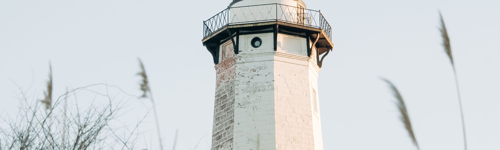 Um farol com base branca e vermelha, rodeado por grama alta.