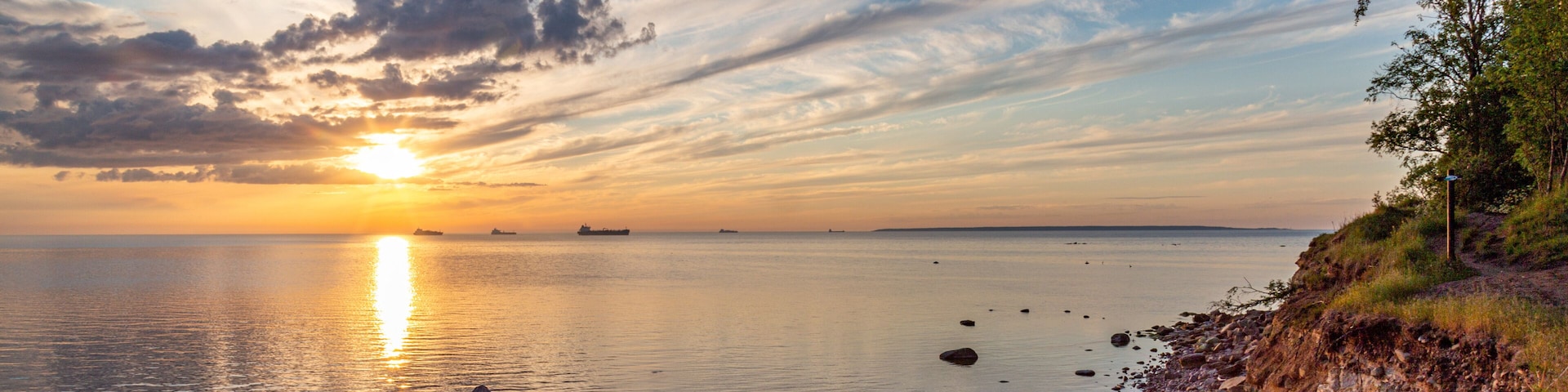 Um pôr do sol sobre um mar calmo, com uma rocha grande em primeiro plano e uma costa rochosa.