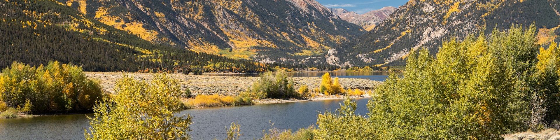 Paisagem montanhosa com um lago e árvores com tons de outono.