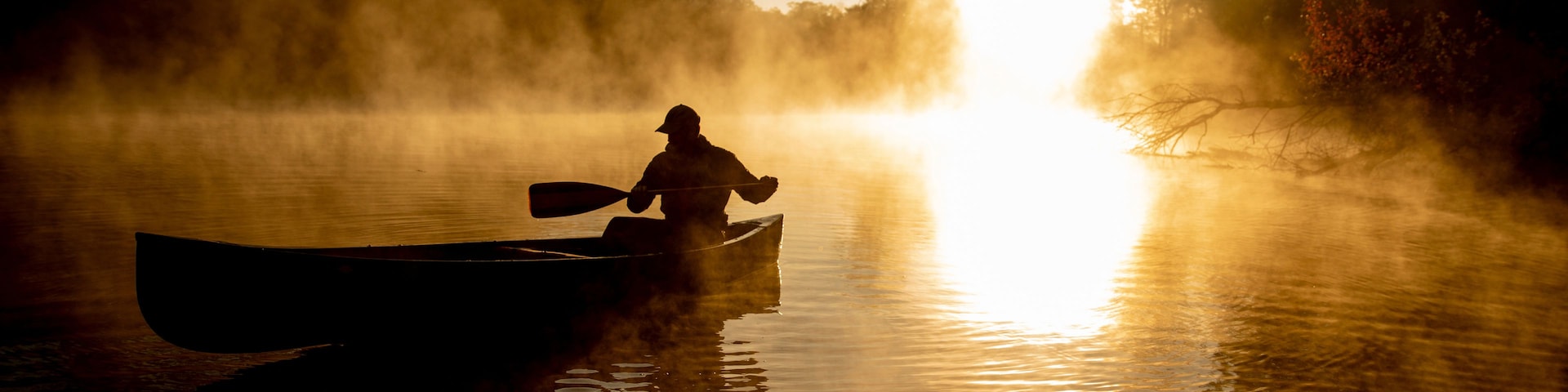Um caiaque em uma canoa em um rio com névoa e árvores nas margens.