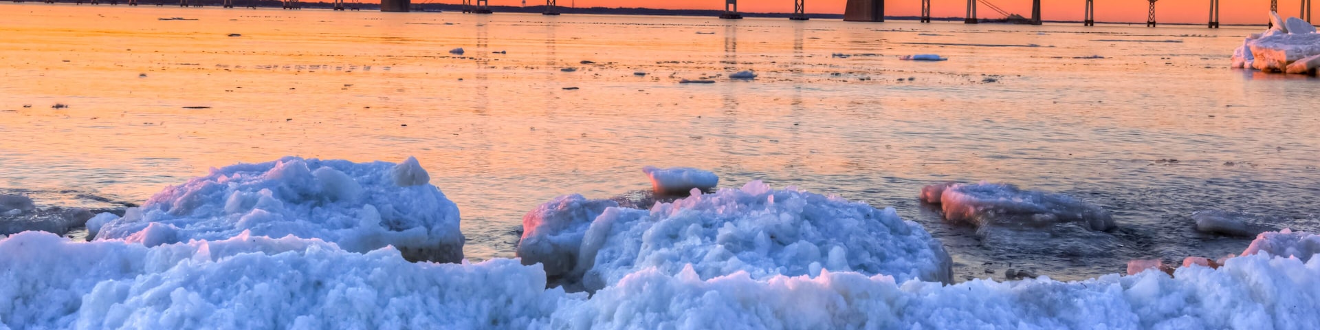Uma ponte sobre um corpo de água congelado ao pôr do sol.