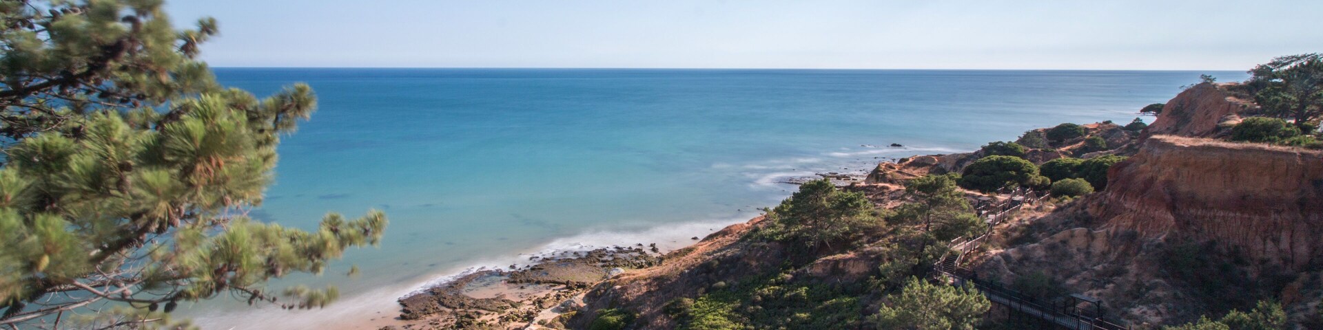 Paisagem costeira com praia, falésias rochosas e vegetação rasteira.