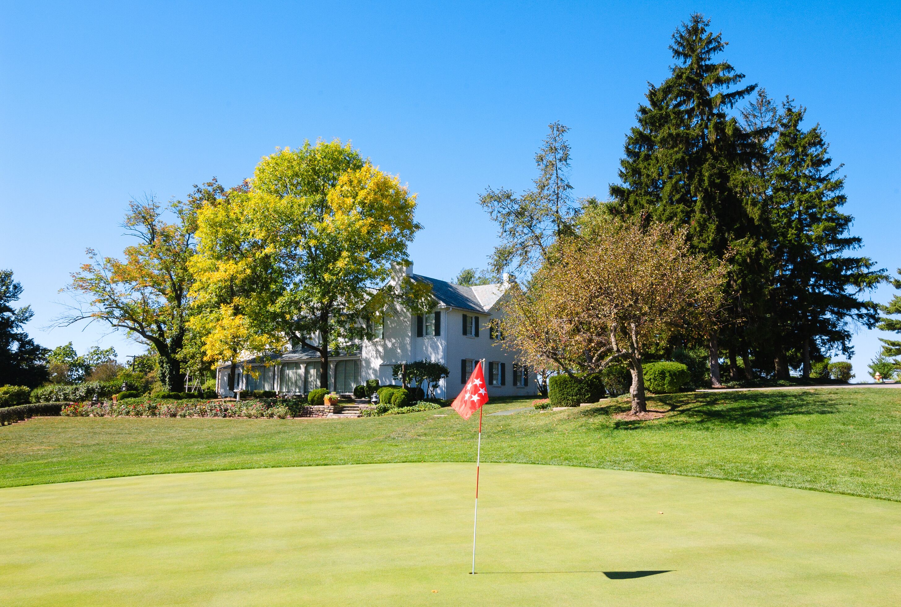 Um campo de golfe com uma bandeira, uma casa e árvores.