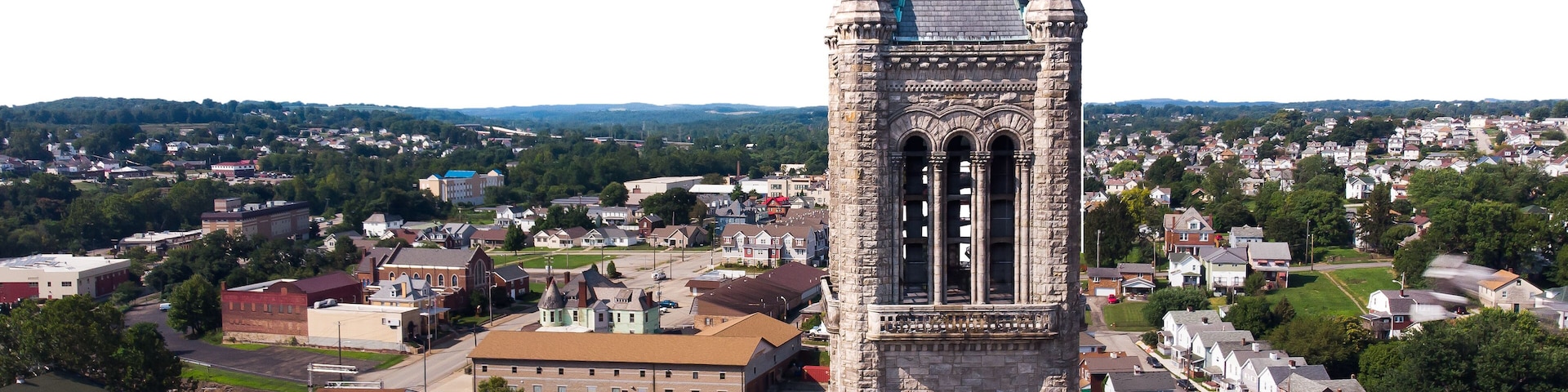 Um campanário com telhado pontiagudo e mostrador de relógio, cercado por uma cidade com vários edifícios e um rio ao fundo.