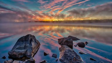 Um pôr do sol sobre um lago tranquilo com pedras em primeiro plano.