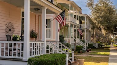 Fileira de casas em tons pastel com bandeiras americanas, corrimãos brancos e gramado bem cuidado.