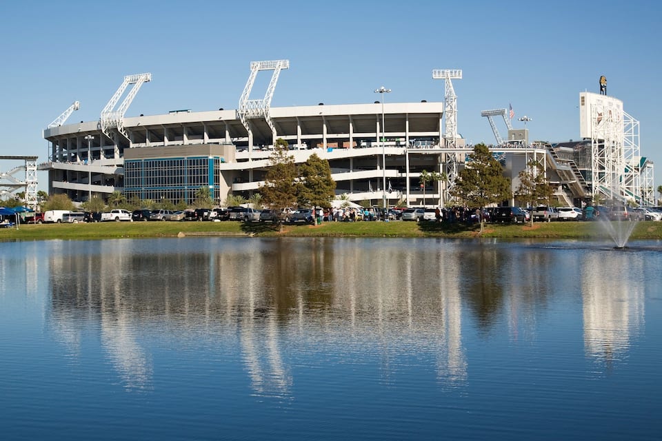 Um estádio com uma grande área de água à frente, refletindo a estrutura.