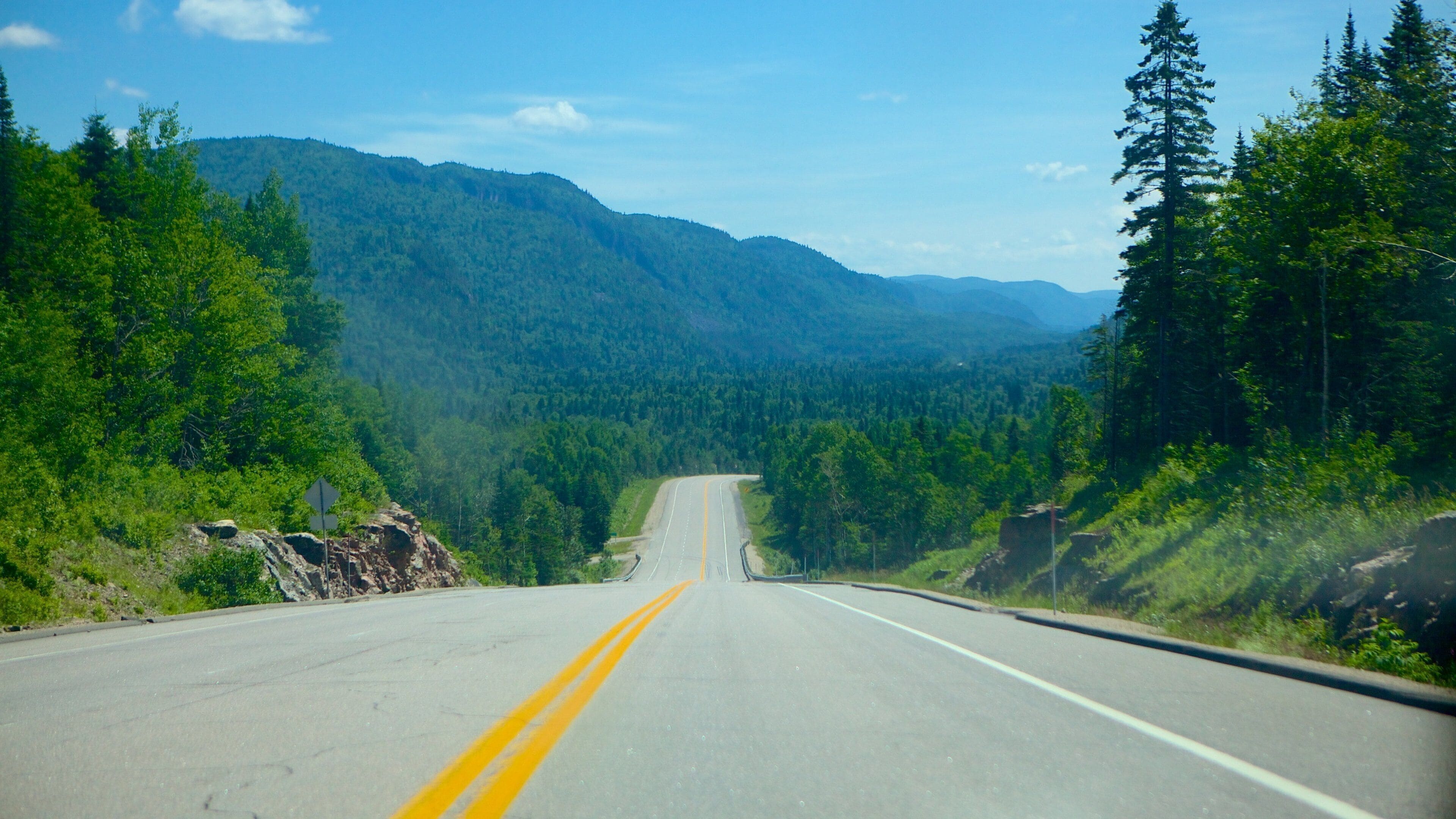 Uma autoestrada de duas faixas ladeada por florestas densas e montanhas.