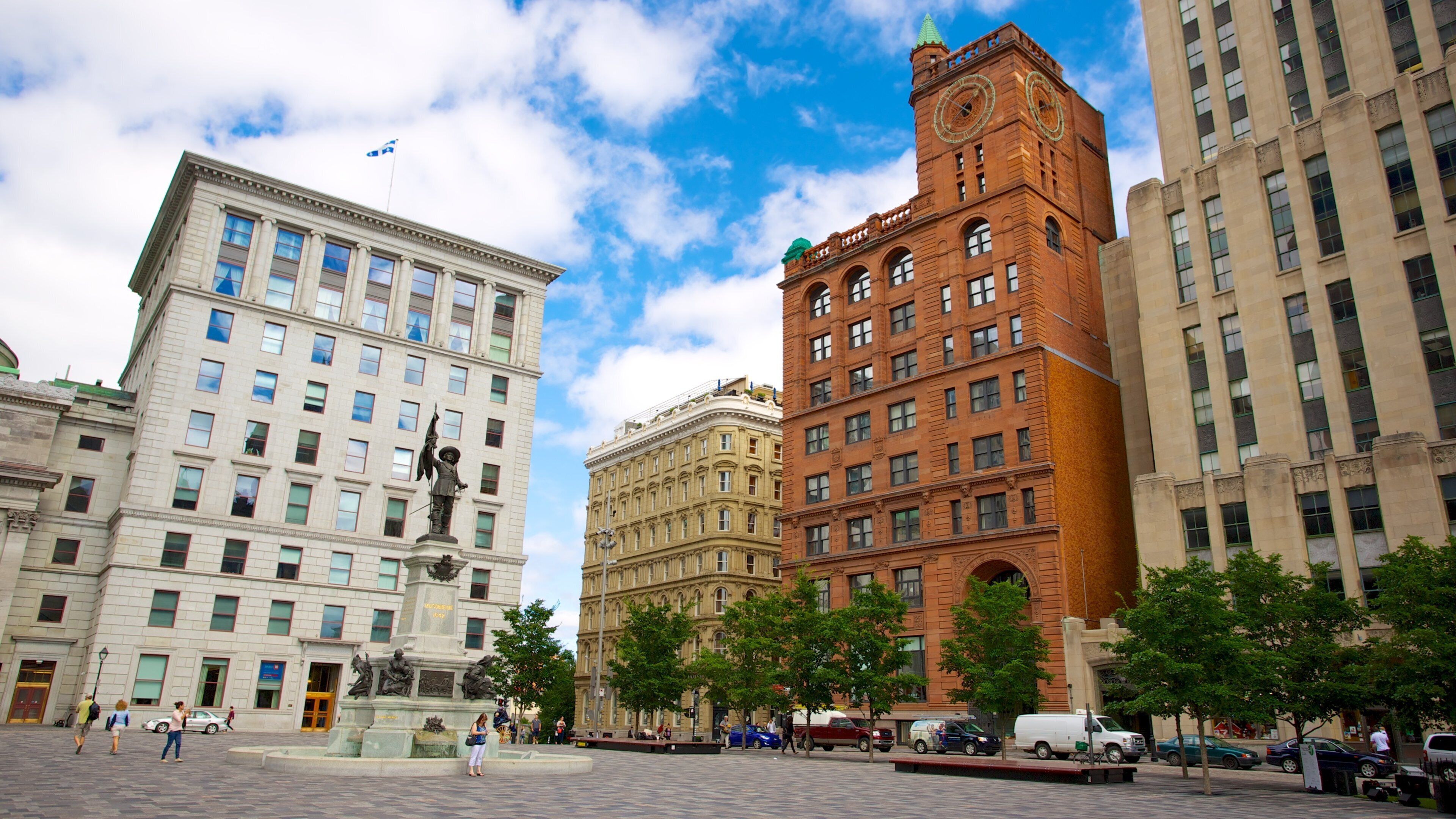 Uma praça urbana com uma estátua, um campanário e edifícios históricos.