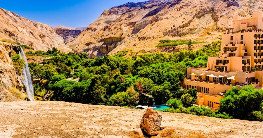 Paisagem montanhosa com cachoeira, vegetação exuberante e um complexo de edifícios modernos.
