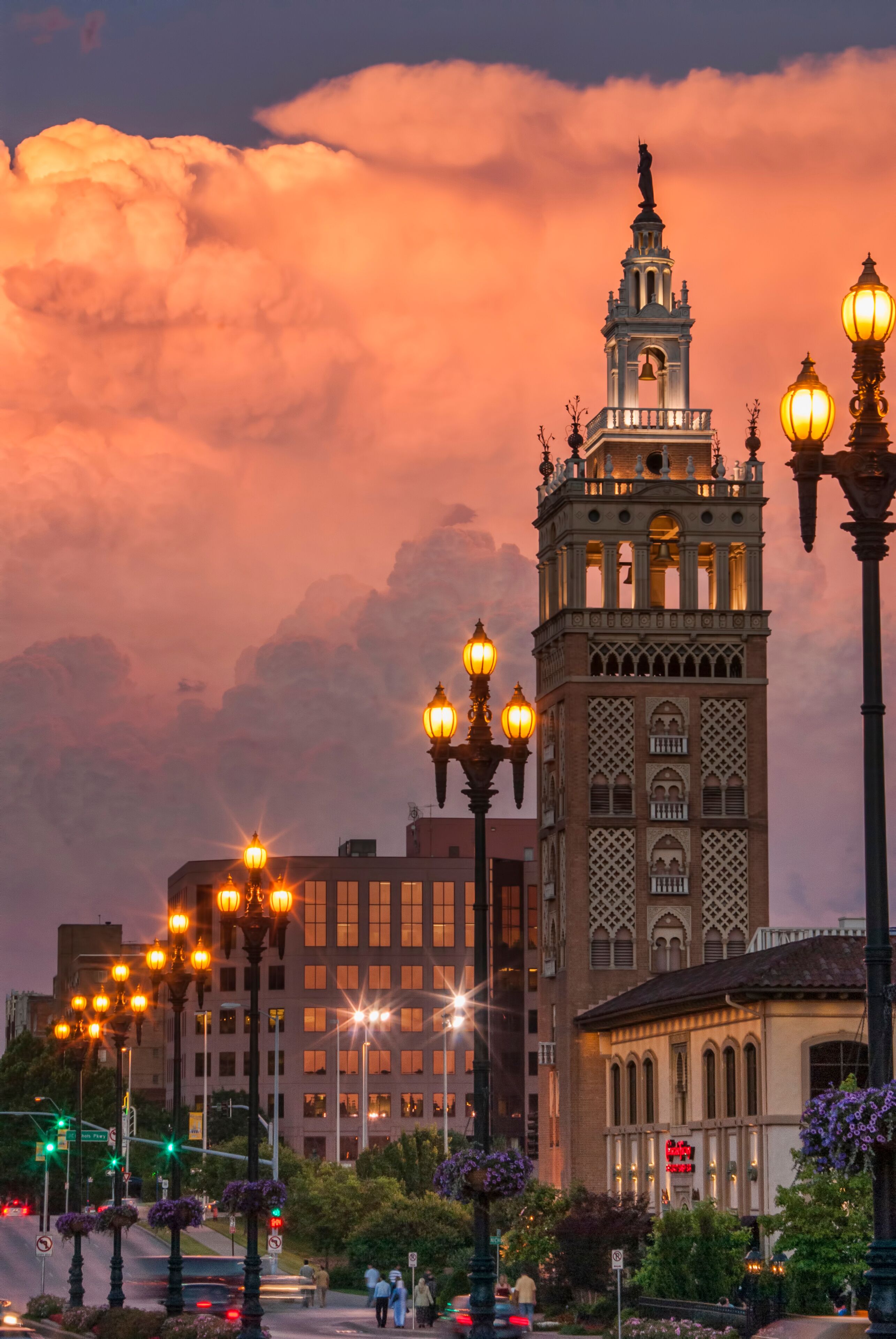 Um edifício histórico com uma torre de sino, luminárias de rua ornamentadas e um céu ao pôr do sol.