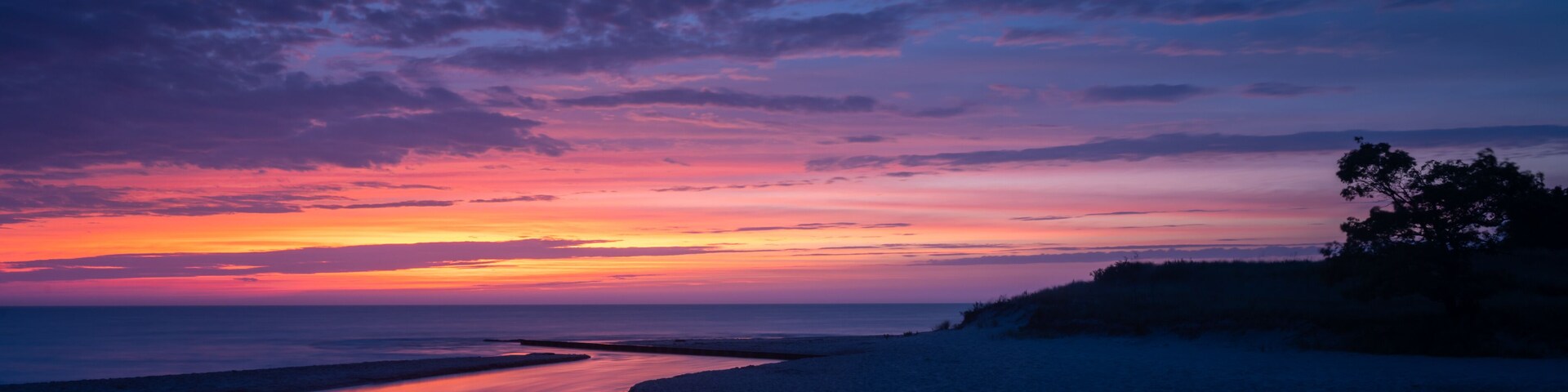 Um pôr do sol sobre uma praia com um mar calmo refletindo o céu.