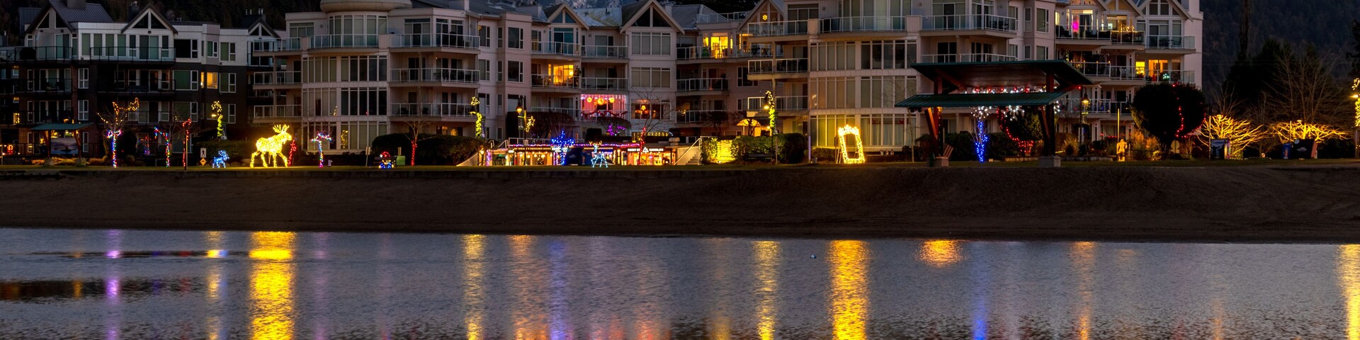 Um resort com montanhas ao fundo, um corpo d'água refletindo a paisagem e edifícios iluminados.