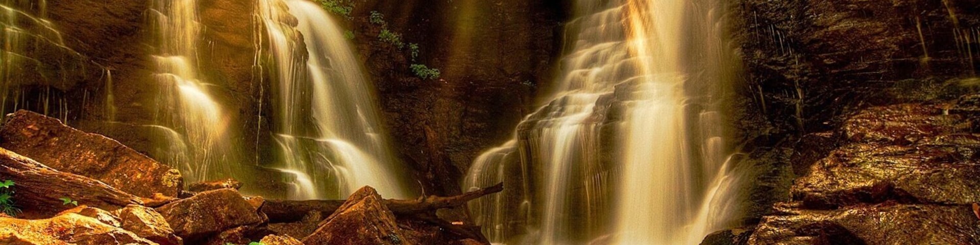 Uma cascata caindo sobre rochas em uma área arborizada.