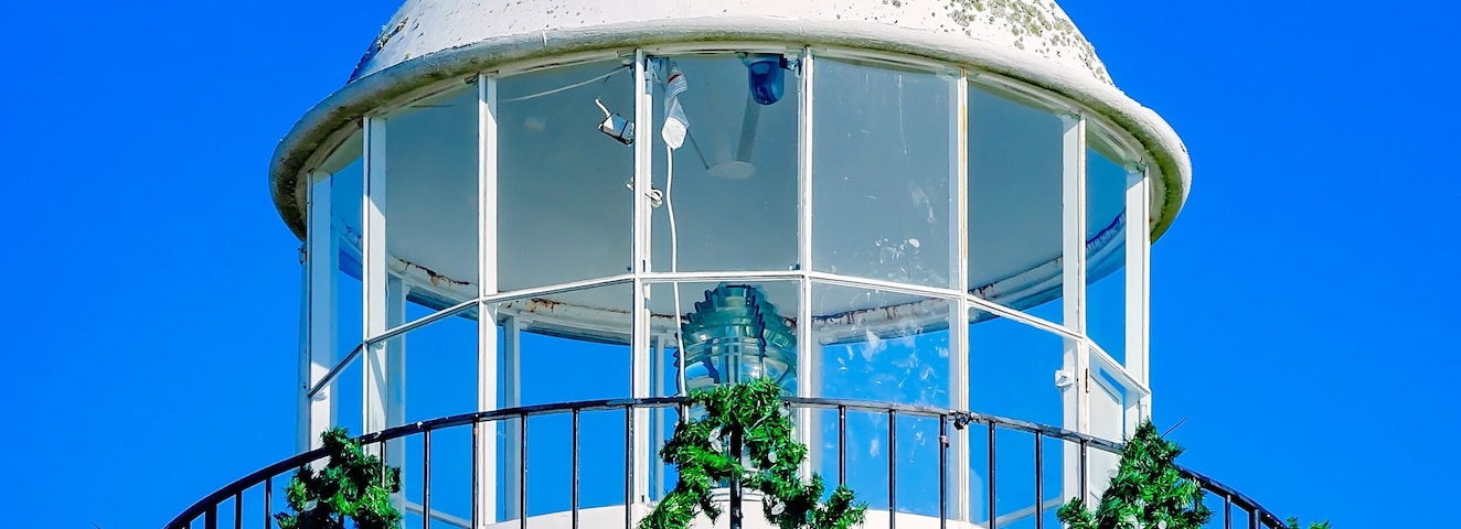 Um farol com uma cúpula branca, um arco vermelho e guirlandas verdes.