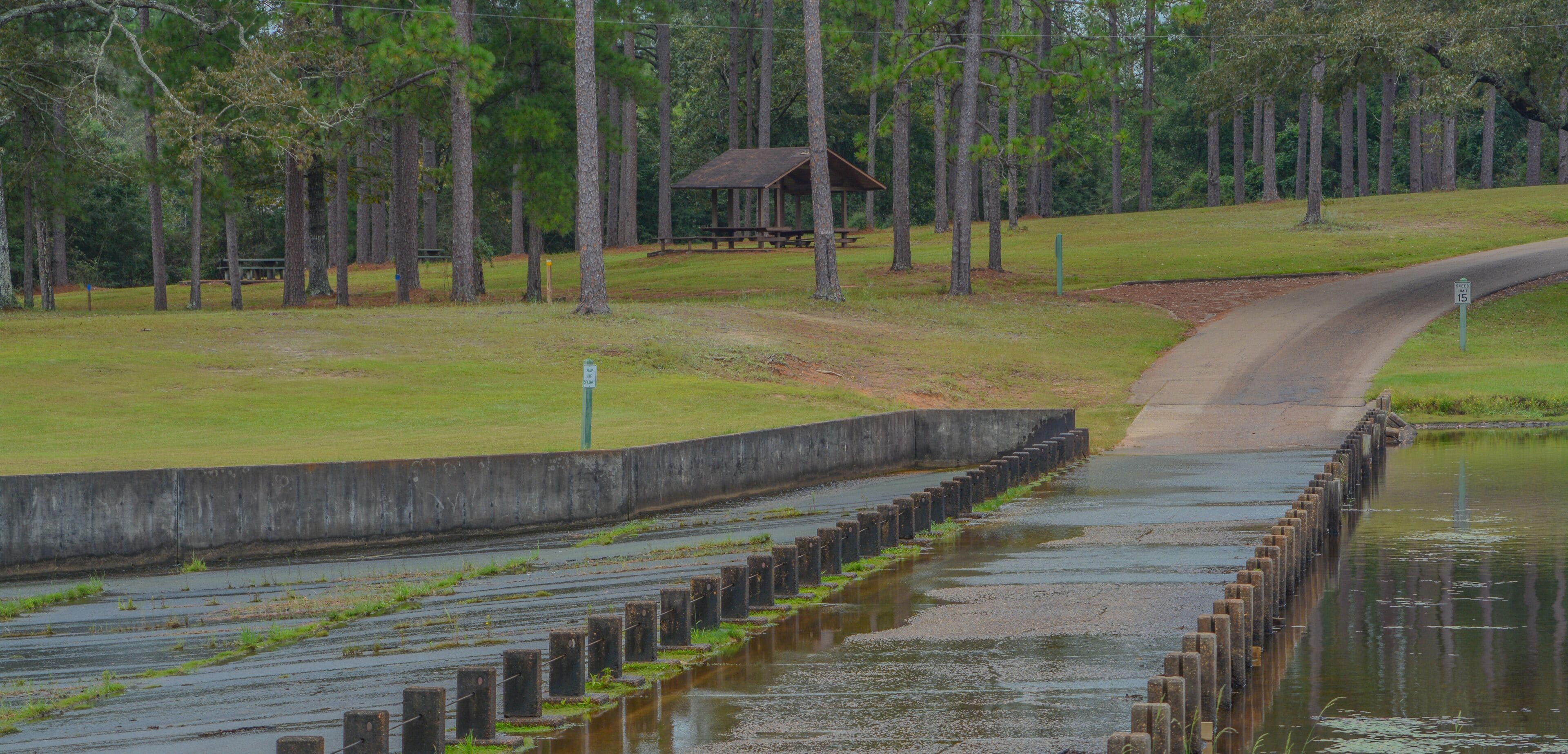 Um parque com um abrigo para piquenique, uma barreira de concreto e uma estrada curva.