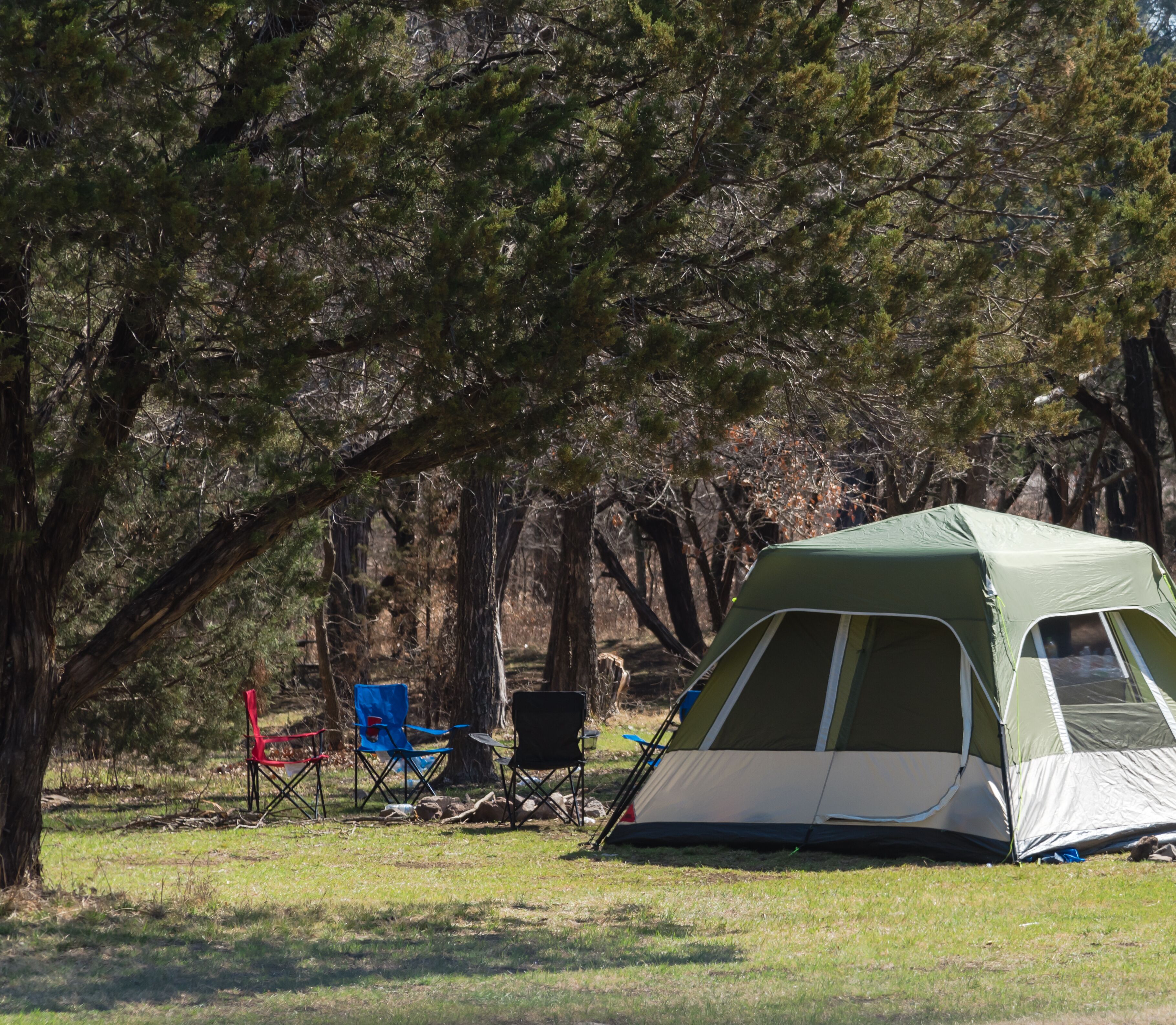 Um camping com uma tenda, duas cadeiras e uma área arborizada.