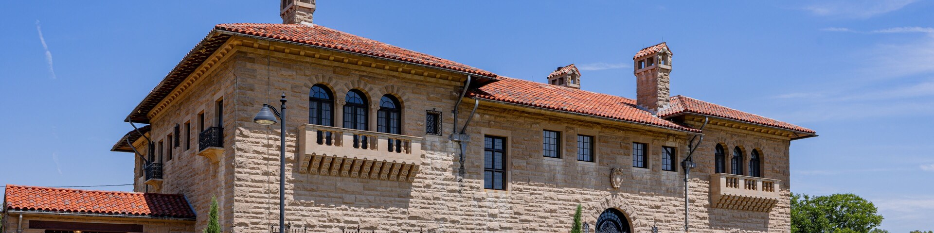 Um edifício de pedra grande com telhado de telhas vermelhas, várias janelas e um gramado bem cuidado.