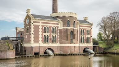 Um edifício histórico de tijolos com janelas em arco e uma chaminé alta, localizado às margens de um canal.
