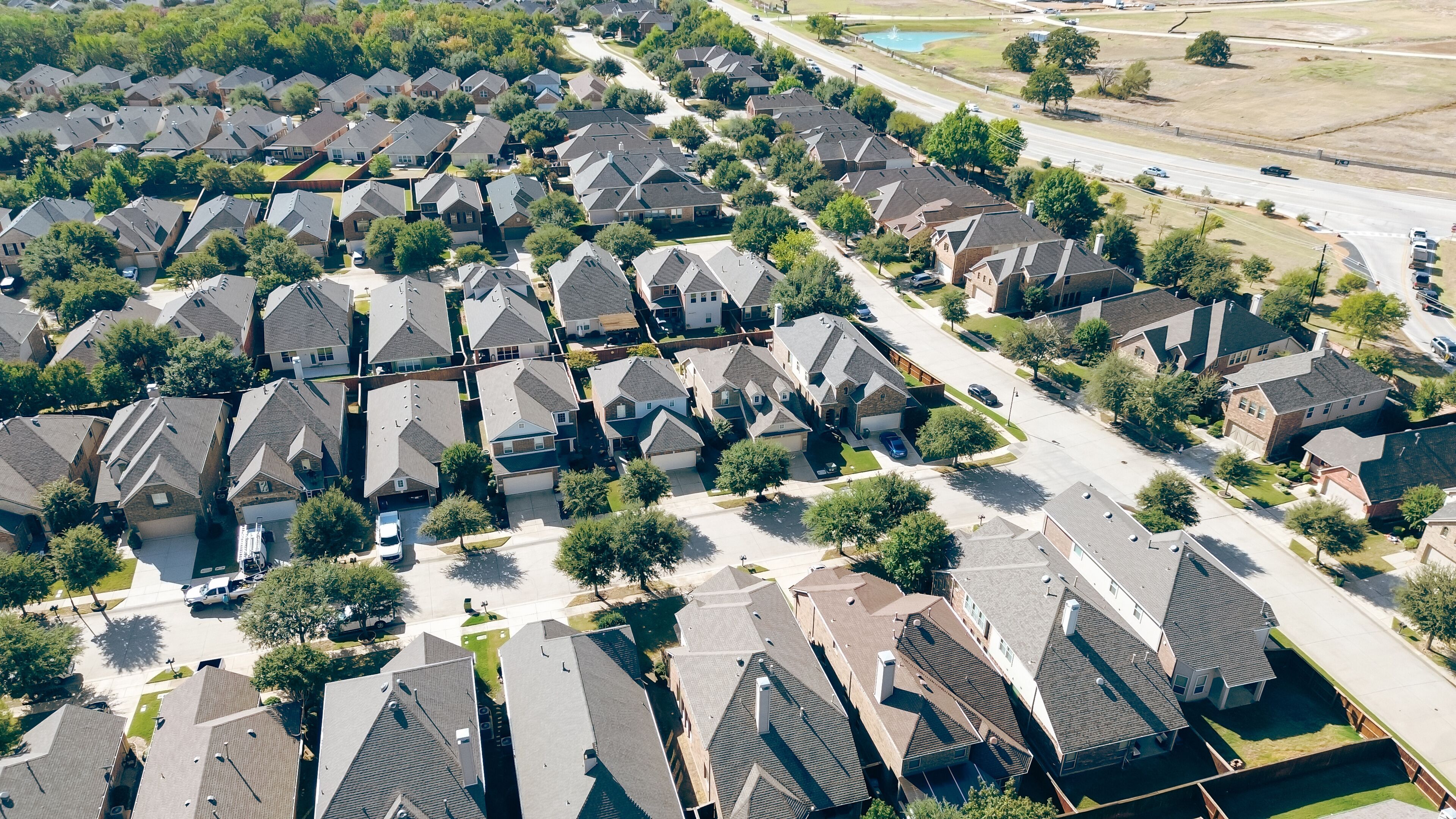 Uma área residencial com casas próximas, uma avenida principal e um grande campo verde ao fundo.