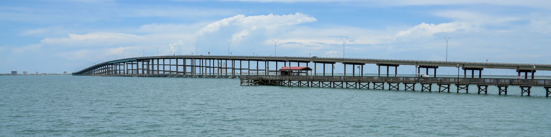 Uma ponte longa e curva sobre a água, com um pequeno pavilhão no lado direito.