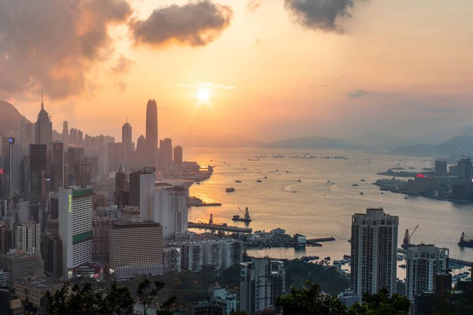 Paisagem urbana com edifícios altos, um corpo d'água e um pôr do sol.