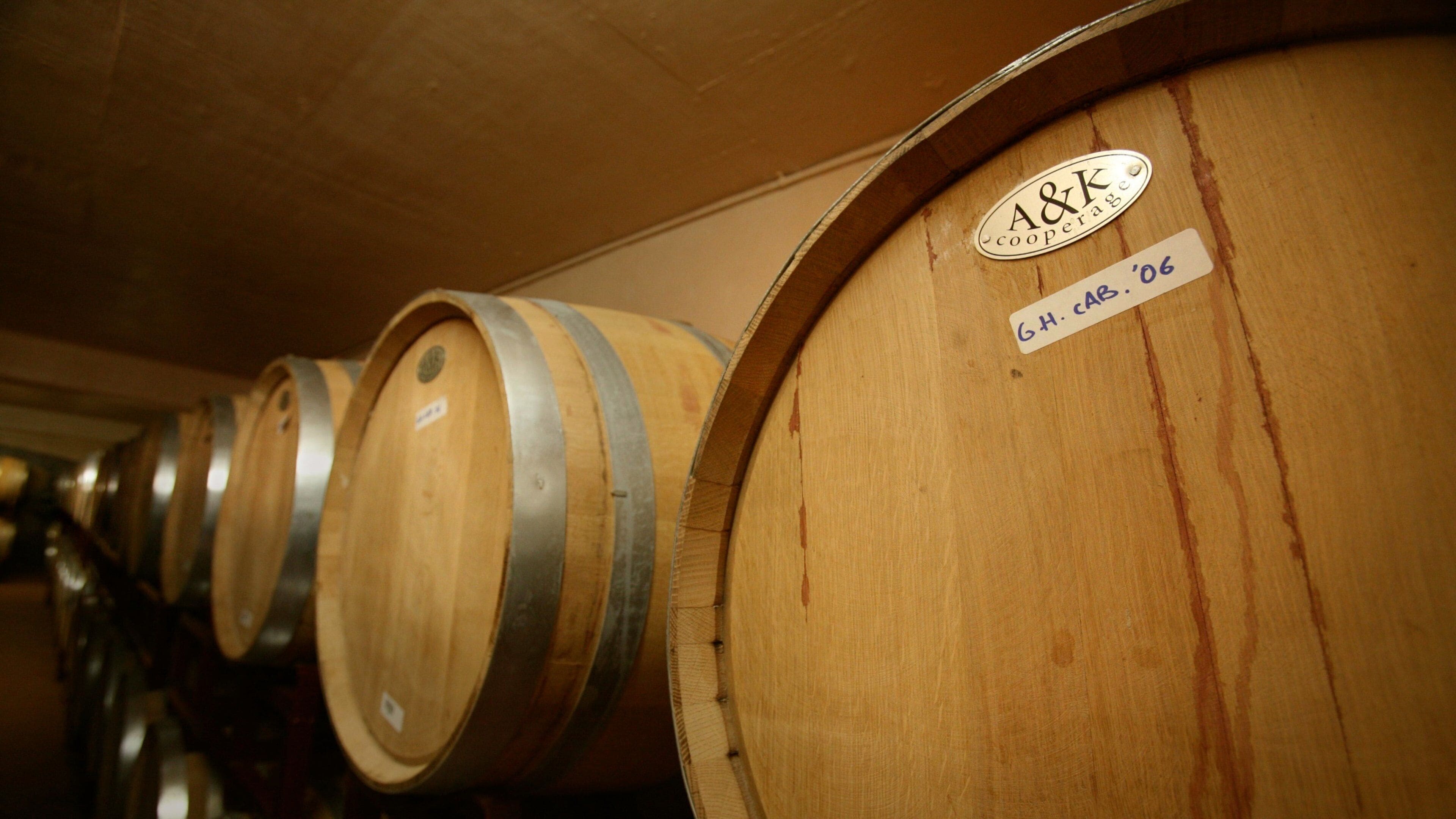 Barris de madeira com faixas e etiquetas de metal, provavelmente utilizados para envelhecer vinho ou destilados.