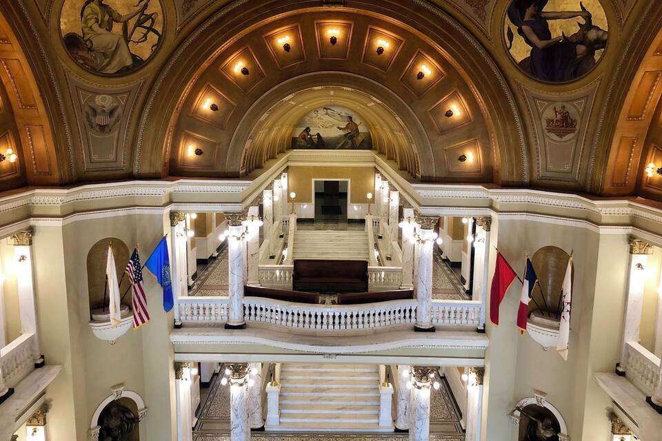 Um interior imponente com uma escadaria de mármore, teto ricamente decorado e bandeiras.