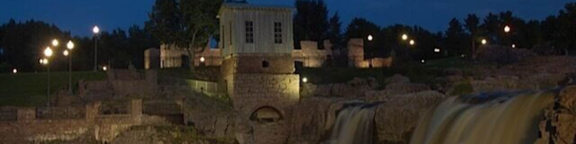 Um edifício histórico de pedra com uma cascata ao primeiro plano.