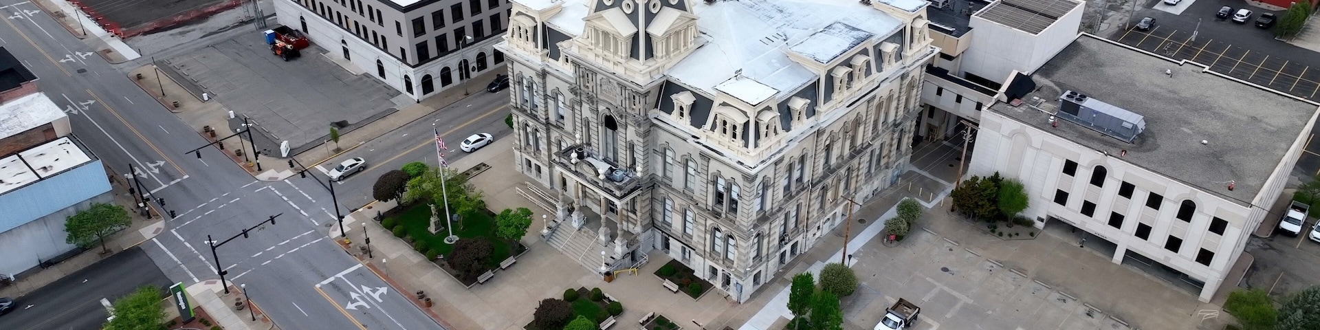 Vista aérea de um edifício histórico com torre do relógio, cercado por ruas e outros edifícios.